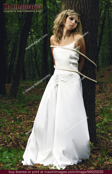 Young bride in wedding dress tied to a tree with ropes in a forest ...
