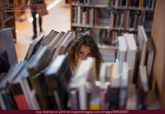 Young woman, college student, looking from behind a book shelf in a ...