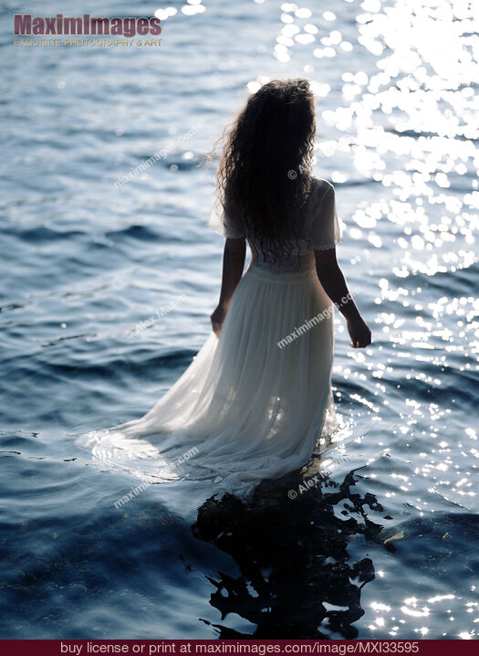 Woman in sheer white dress standing in the water in sunshine. Stock ...